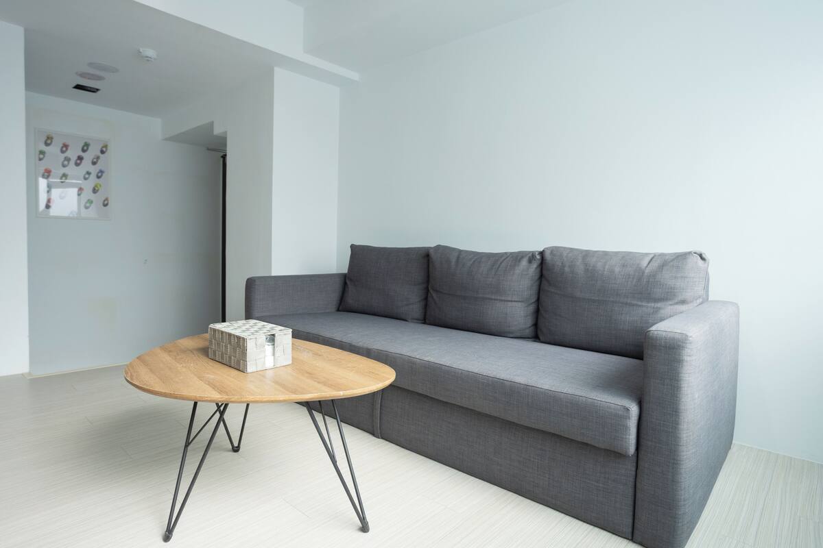 Uma sala de estar moderna com um sofá cinzento, uma mesa de centro de madeira e piso em tons claros.