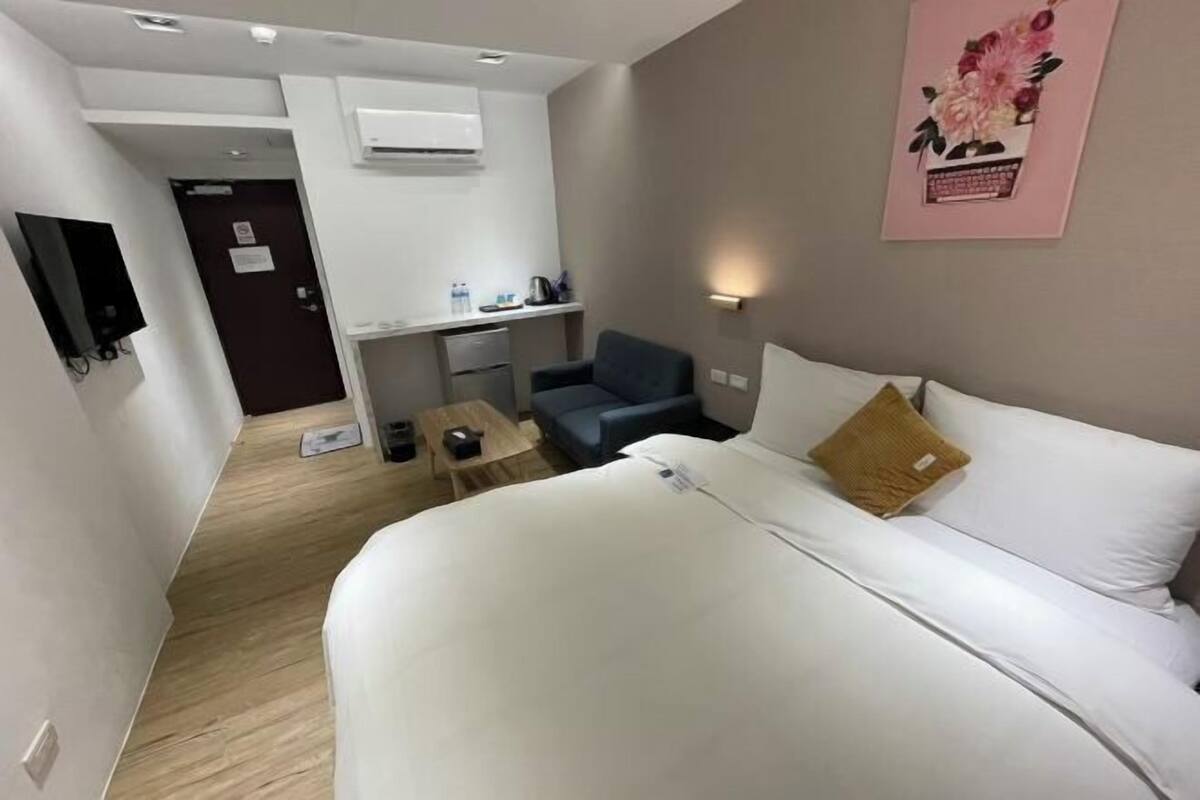 Quarto de hotel com cama, escrivaninha, cadeira e uma mesinha.