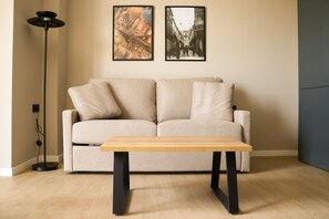Uma sala de estar com um sofá bege, uma mesa de centro de madeira e duas molduras com quadros na parede.