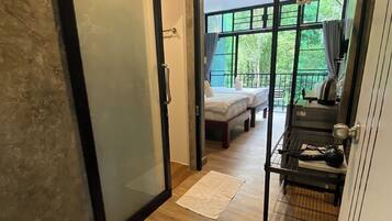 Corredor com porta deslizante que dá para uma varanda com cama e mesa. Há um suporte de metal com uma xícara.