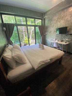 Quarto com cama, escrivaninha, cadeira, televisão e janela com cortinas.