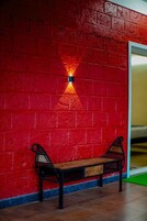 Um banco encostado em uma parede de tijolos vermelhos, com um luminária fixada na parede.