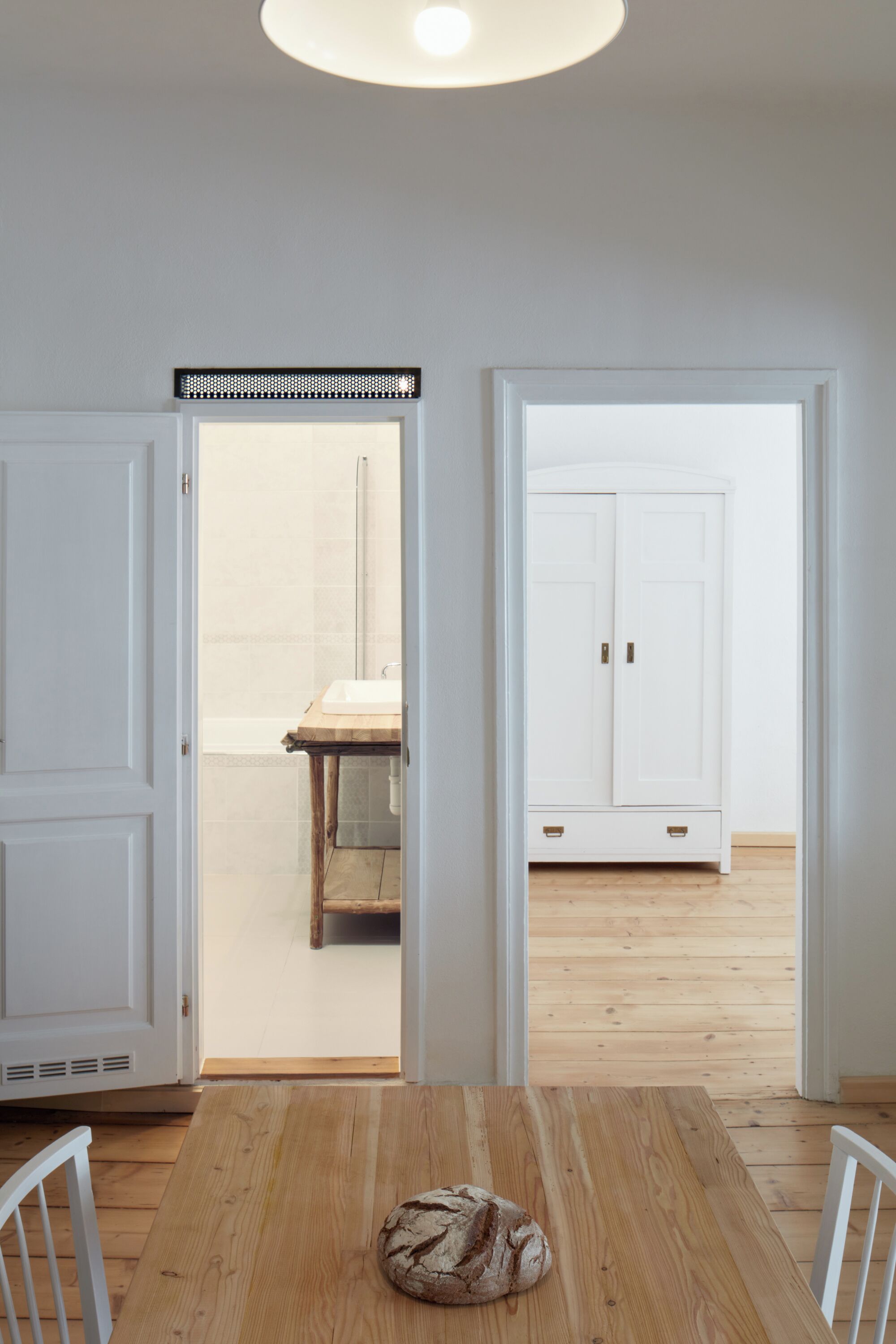 Um quarto com uma mesa de madeira, um pão e um guarda-roupa branco.
