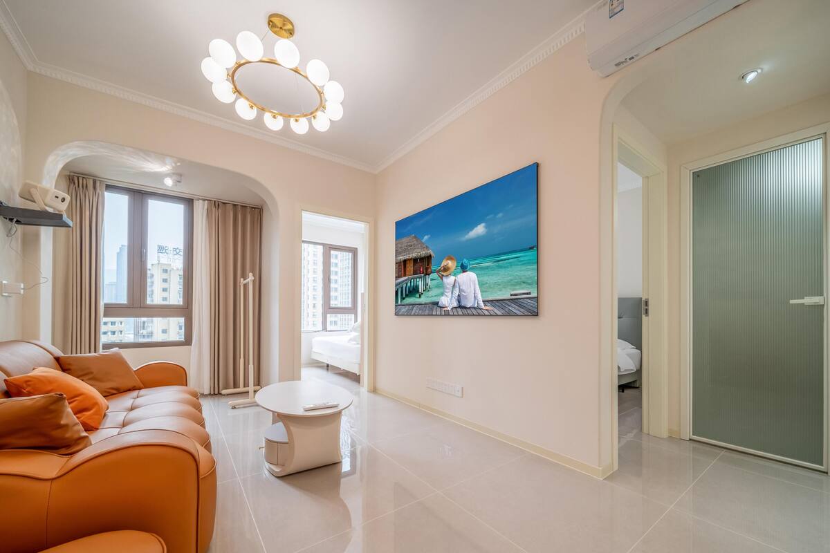 Quarto de hotel moderno com sofá de couro, mesa de centro redonda, pintura de uma praia e uma janela grande com vista para a cidade.