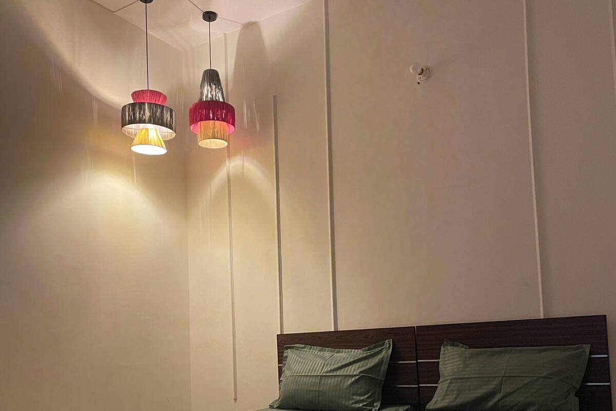 Quarto com cama, duas luminárias pendentes e cabeceira de madeira.