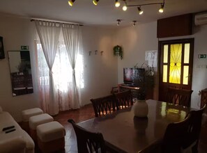 Uma área de refeições com mesa, cadeiras, televisão e janela com cortinas.