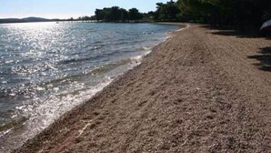 Uma praia de pedrinhas com céu claro e árvores ao longe.