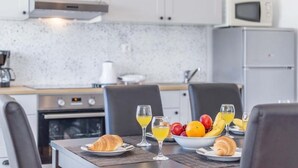 Cozinha moderna com mesa de jantar posta para o café da manhã, incluindo croissants, frutas e copos de suco.
