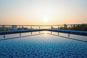 Piscina com azulejos e vista para o céu e edifícios ao longe.