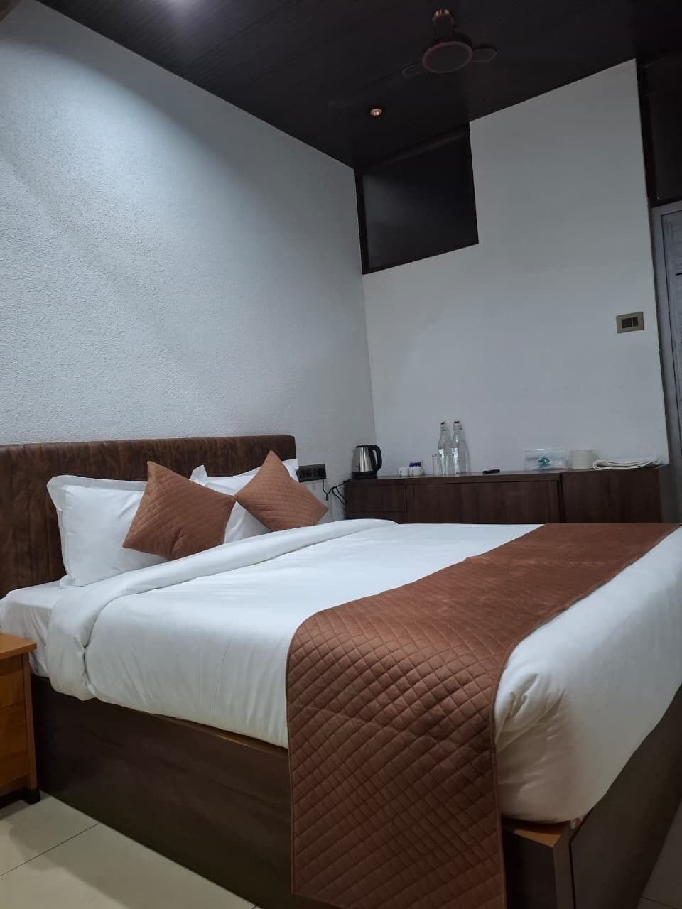 Quarto de hotel com cama, cabeceira de madeira, mesa de cabeceira e criado-mudo.