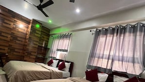 Quarto de hotel com duas camas, ventoinha no teto, parede de destaque em madeira e janela com cortinas.