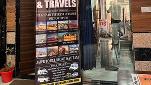 Um saguão de hotel com um destaque para o cartaz da Royal Raj Tour & Travels, um escritório visível e uma área de sanitários identificada.