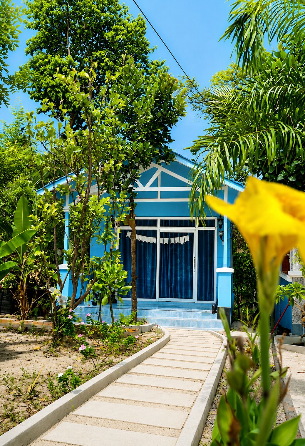 Uma casa com fachada azul, varanda frontal e um caminho que leva à entrada.