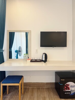 Quarto com televisão de tela plana, uma pequena mesa com uma cadeira, chaleira e uma caixa de chá nano prata.