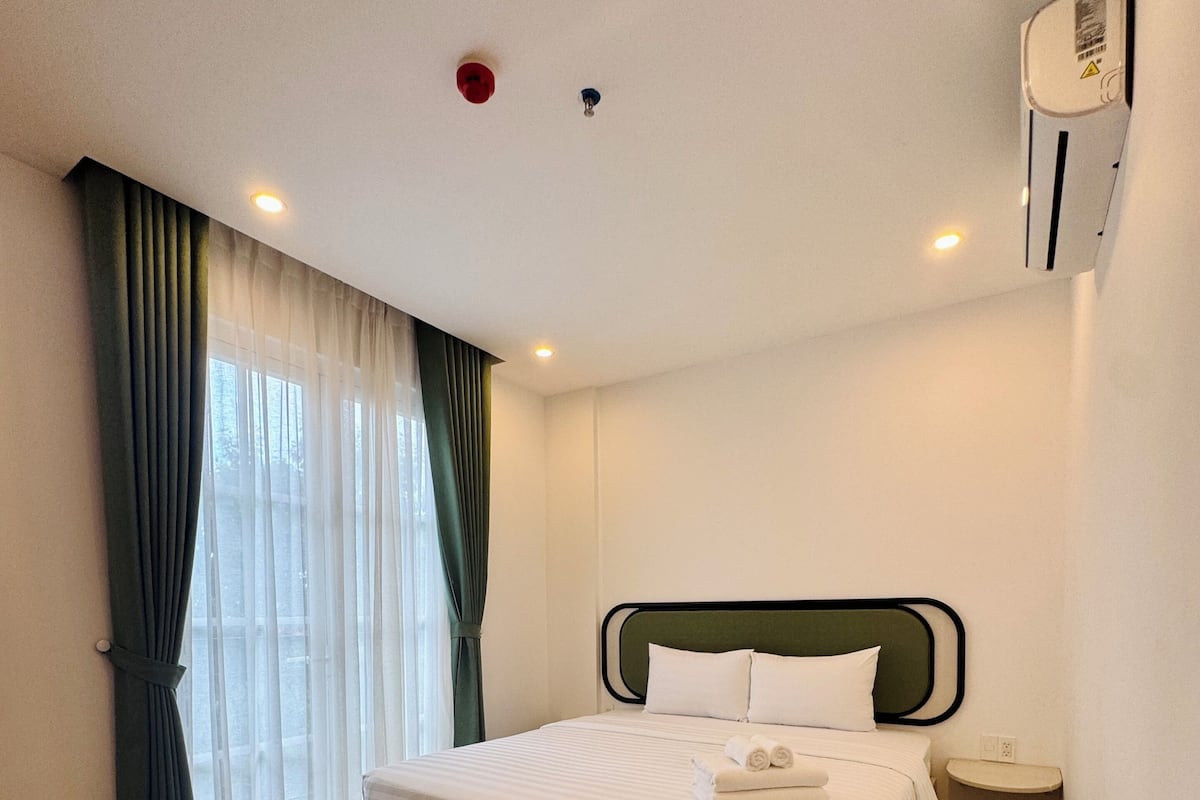 Quarto de hotel com cama, mesa de cabeceira, cortinas e ar condicionado.