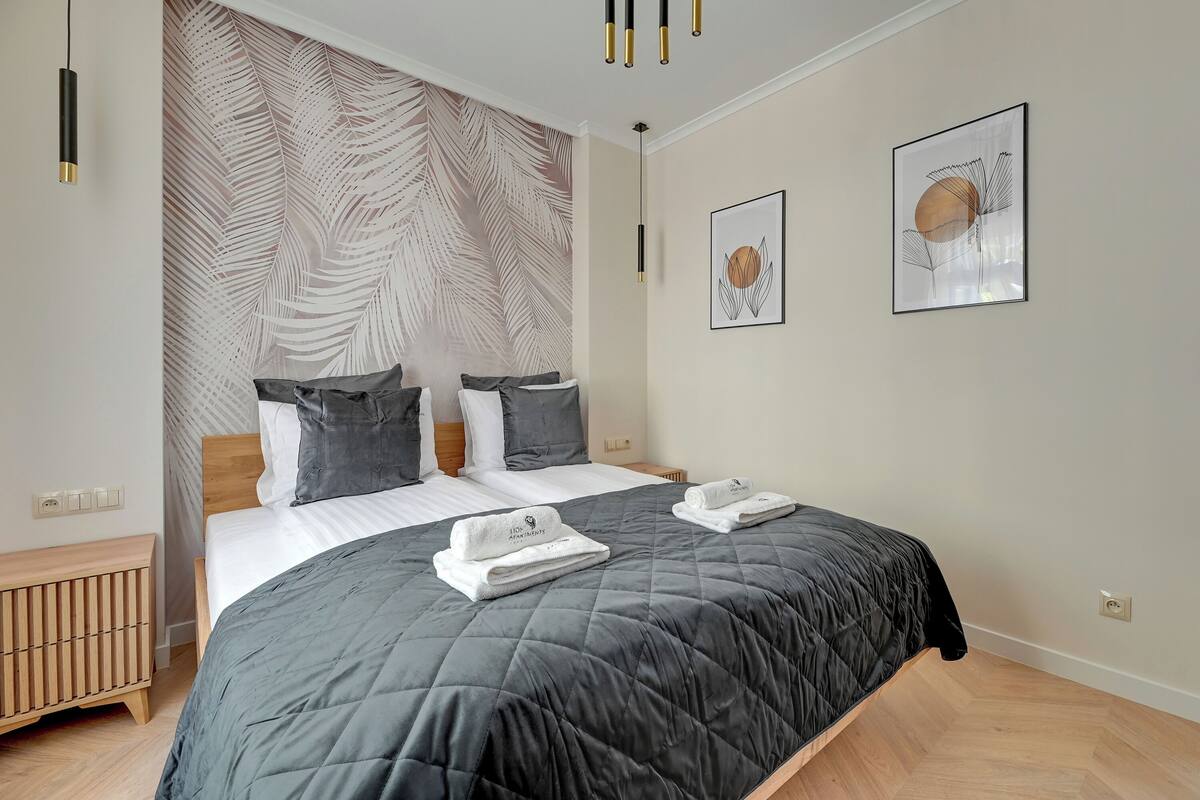 Uma cama bem arrumada com um edredom escuro, uma cabeceira de madeira e papel de parede com padrão de folhas.
