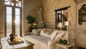 Uma sala de estar acolhedora com sofá, mesa lateral com luminárias, uma estátua decorativa e uma janela com vista.