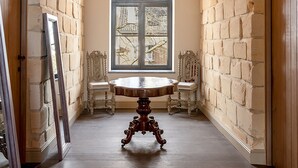 Quarto com teto de madeira, um candelabro, uma janela grande e duas cadeiras antigas.