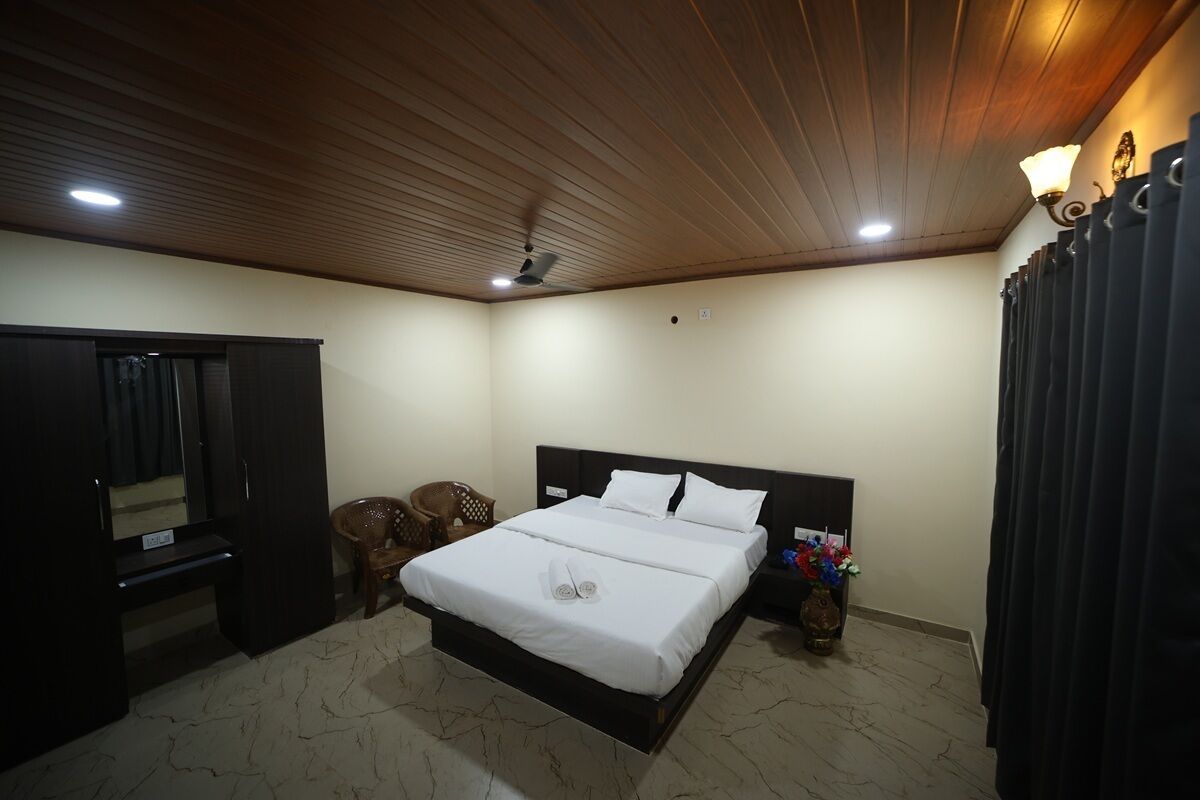 Quarto de hotel com cama, escrivaninha, cadeira, mesa de cabeceira e ventoinha no teto.