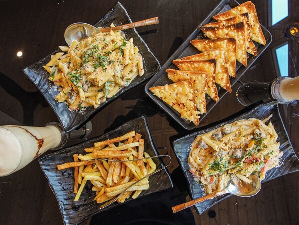 Uma mesa com quatro pratos: massa com queijo, queijo grelhado, batatas fritas e outro prato de massa.