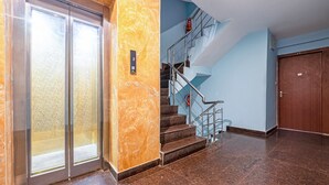 A hotel lobby with a marble staircase, a fire extinguisher, and a door with a number plate.
