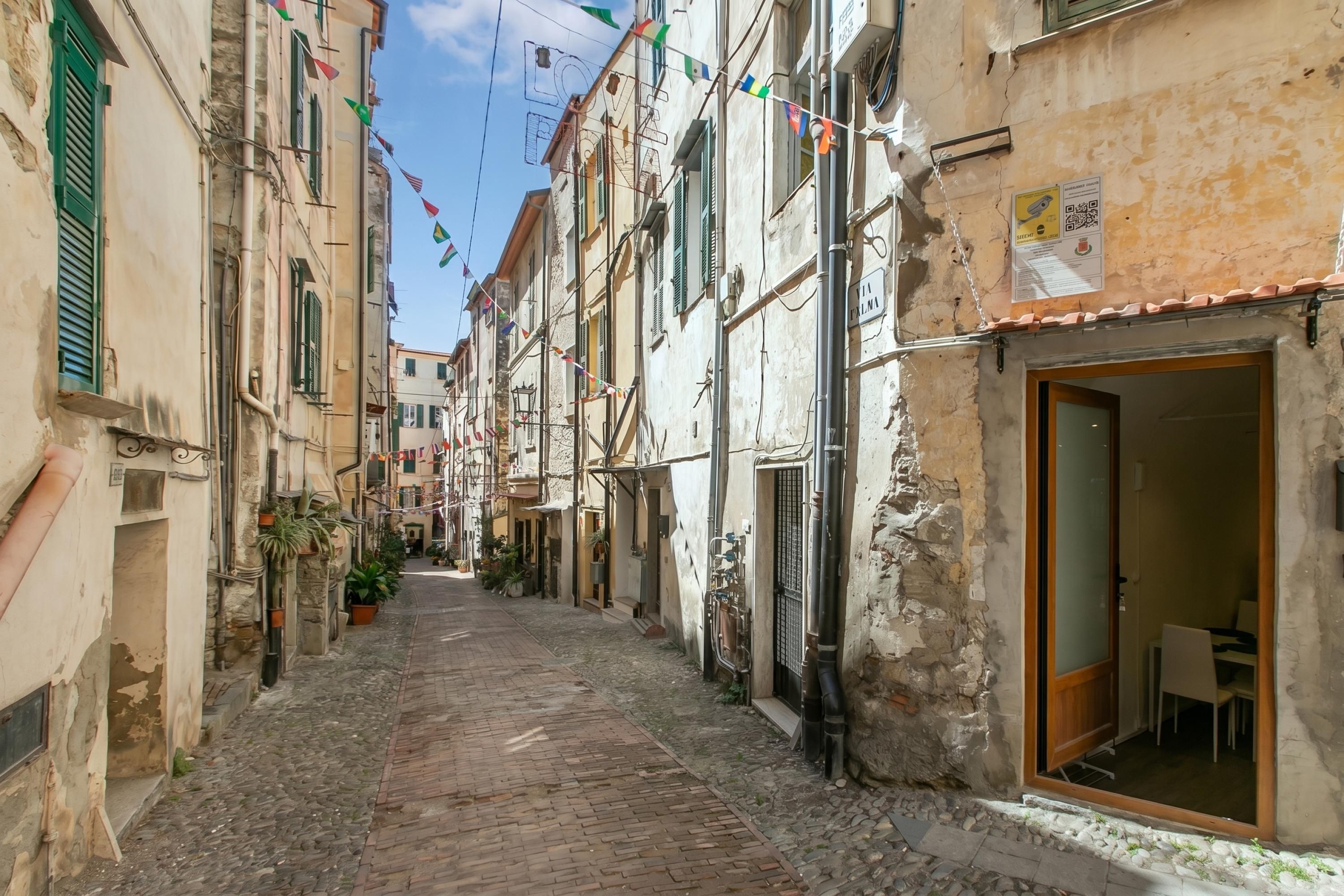 Uma rua de calçada estreita, ladeada por edifícios históricos com varandas e plantas em vasos.