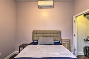 Quarto com cama, mesa de cabeceira, ar condicionado fixado na parede e porta que dá para um armário.