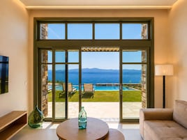 Quarto com uma grande porta de correr de vidro que dá para uma área de piscina ao ar livre, com vista para o mar e montanhas.