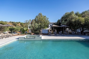 Uma piscina com espreguiçadeiras e guarda-sóis, cercada por árvores e edifícios.