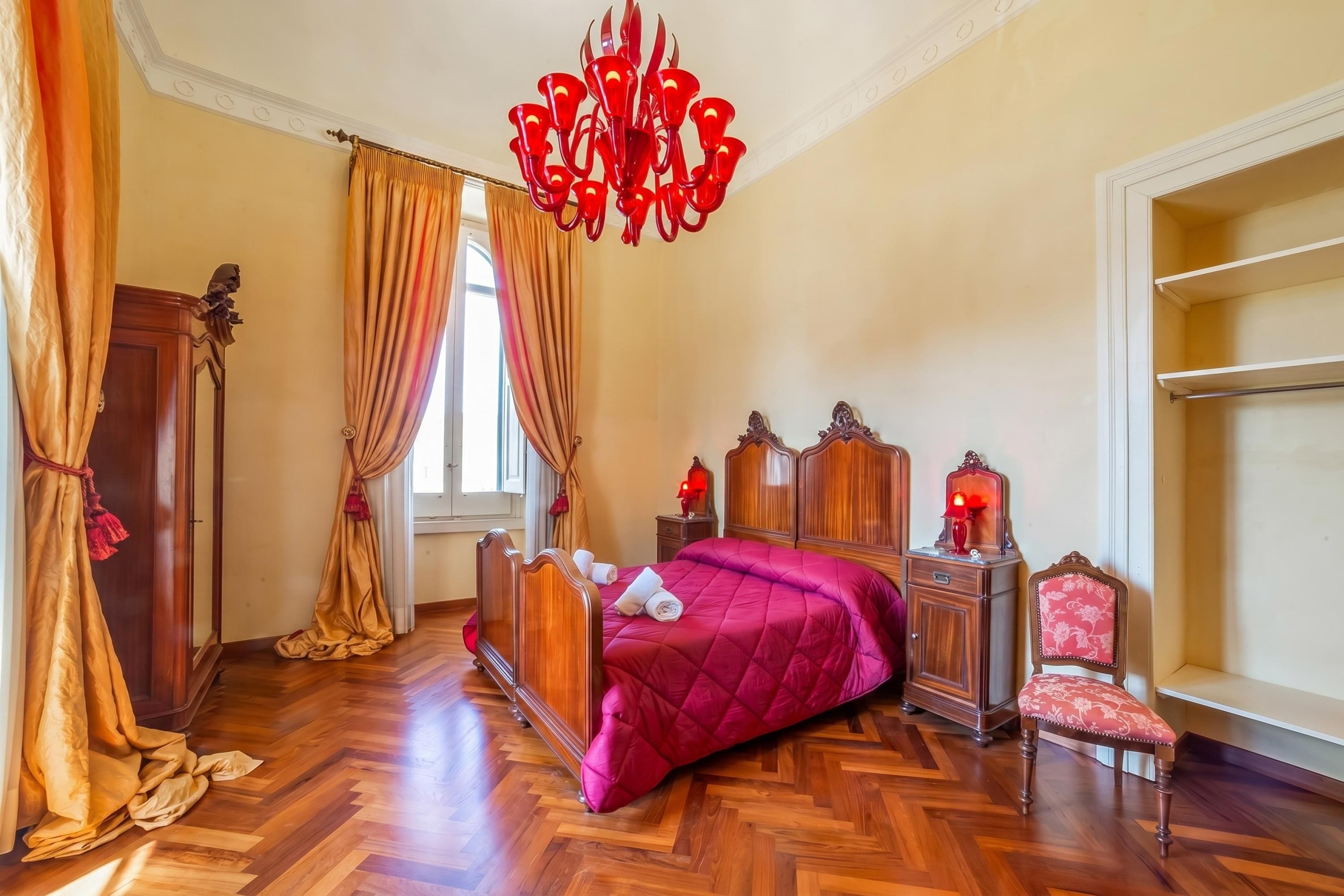 Quarto com cama de madeira, um lustre vermelho, mesa de cabeceira de madeira e uma cadeira.