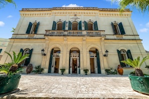 Um edifício histórico com fachada simétrica, grandes janelas em arco e uma entrada central.