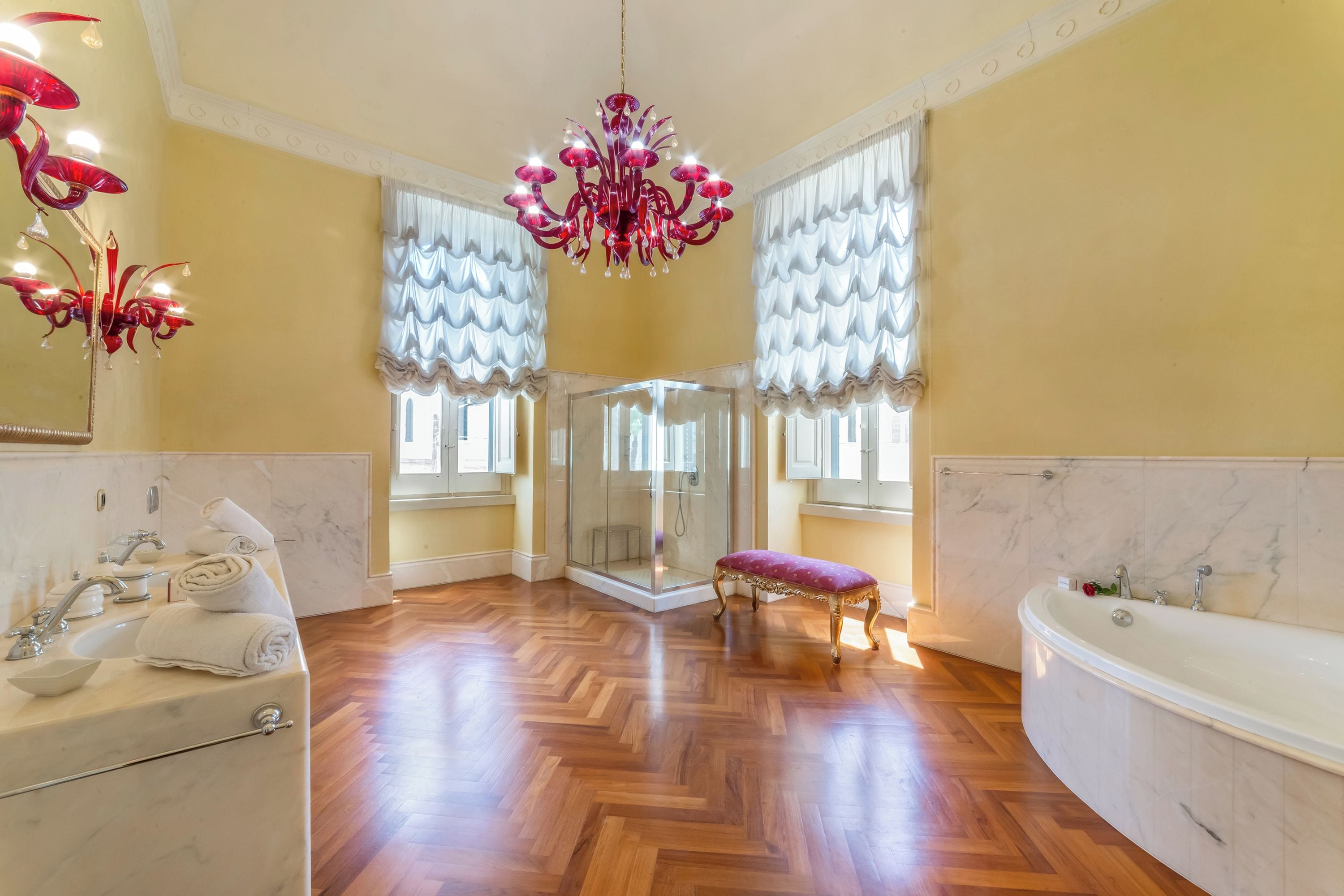 Um banheiro espaçoso com pia de mármore, banheira de pedestal, um banco e box de vidro.