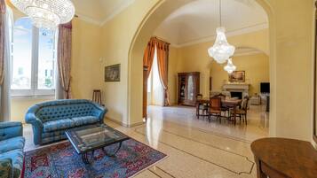 Uma sala de estar ampla, com um sofá azul, uma mesa de centro de vidro e um tapete estampado.