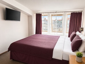 Quarto de hotel com cama grande, televisão de tela plana na parede e janela com cortinas.