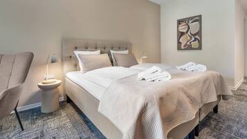 Quarto de hotel com cama, poltrona, mesa de cabeceira, abajur e um quadro na parede.