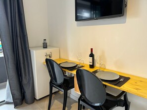 Uma pequena área de refeições com uma televisão na parede, uma garrafa de vinho e dois copos sobre uma mesa de madeira.