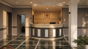 Uma área de recepção com piso de mármore, balcão de atendimento, um objeto decorativo na parede e um vaso de planta.