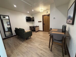 Um espaço compacto com sofá, mesa de jantar, televisão na parede e porta que dá para outro quarto.