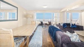 Um quarto espaçoso com uma grande mesa de jantar, um conjunto de sofás e vista para o mar por grandes janelas.