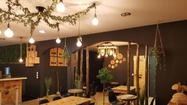 Interior de restaurante com mesas de madeira, lâmpadas pendentes e decoração rústica.