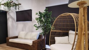Quarto com sofá de vime, cadeira suspensa, planta em vaso e luminária.