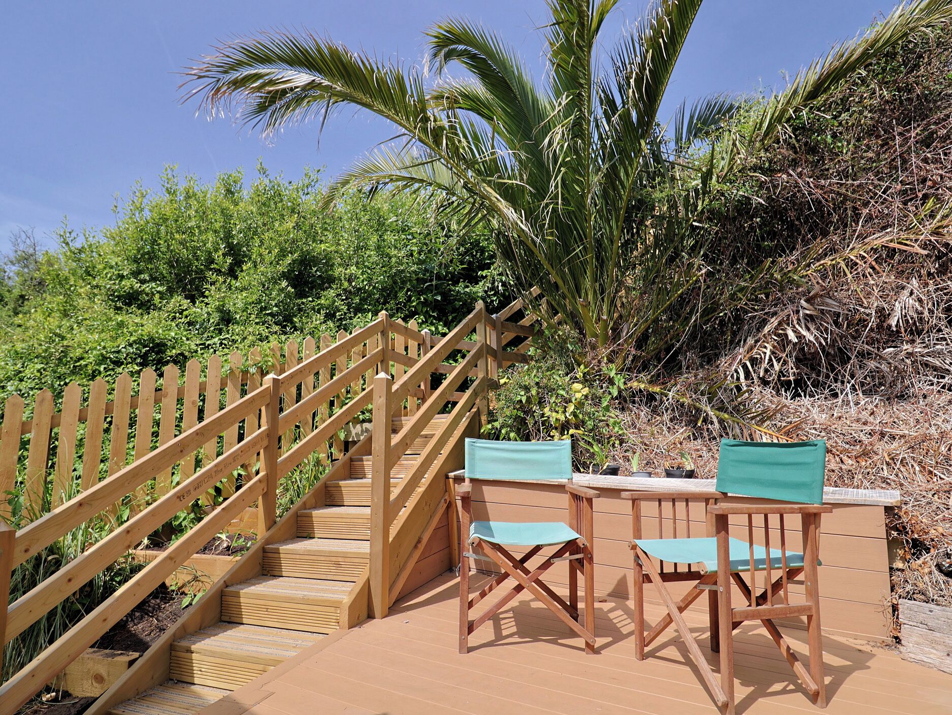 Escada de madeira que leva a um deck com duas cadeiras e uma mesa.