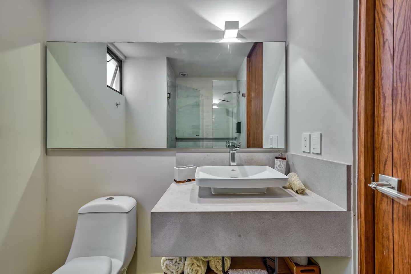 Casa de banho moderna com um espelho grande, uma sanita branca e uma casa de banho.