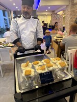 Um chef servindo uma sobremesa com bolachas em um prato com a etiqueta 'TATLI MUZLU MAGNOLIA'.