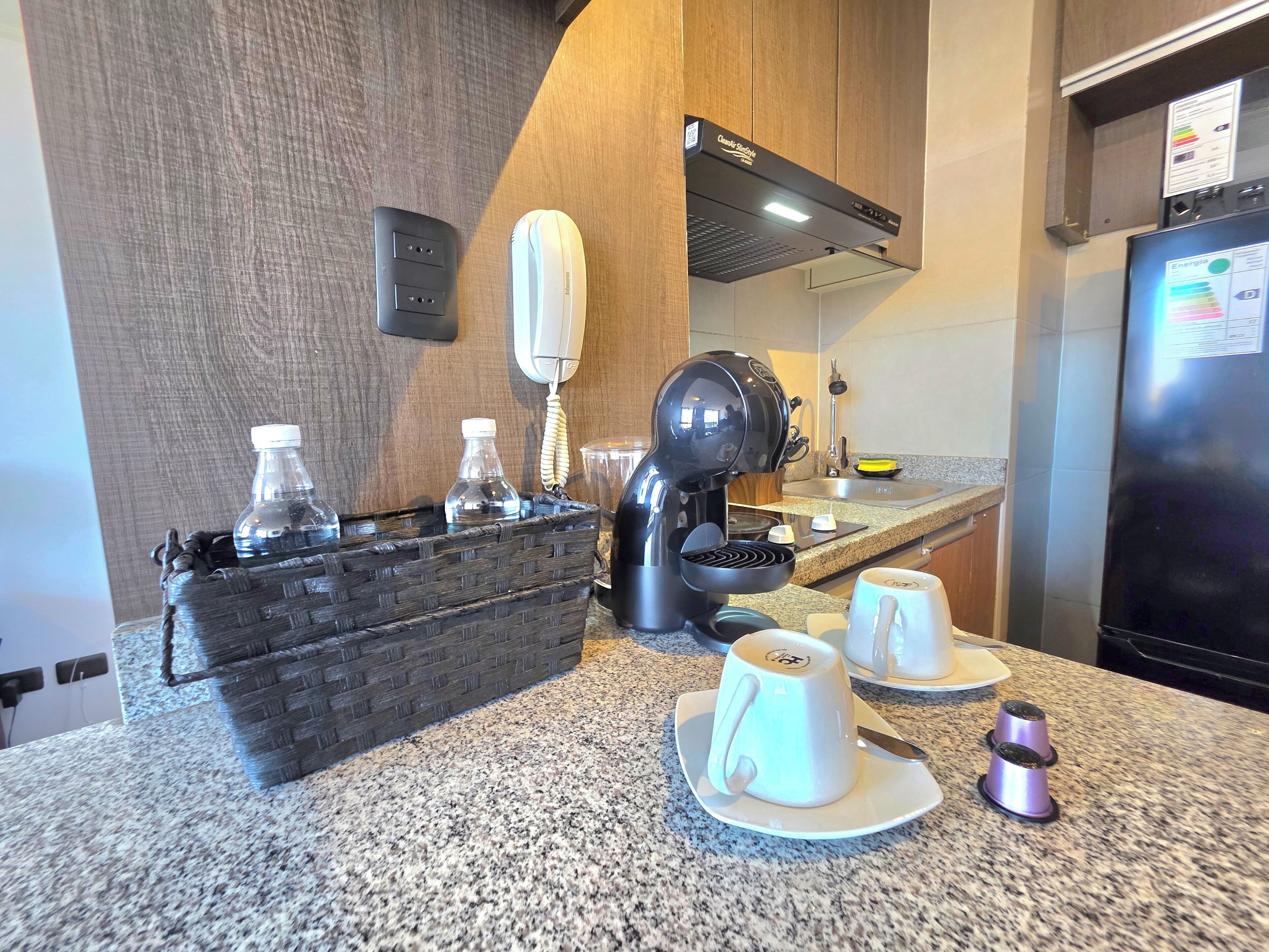 Uma cozinha com cafeteira, chaleira, micro-ondas e geladeira.