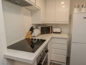 Cozinha compacta com fogão, micro-ondas, torradeira e armários brancos.