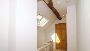 Um corredor com porta de madeira, corrimão branco e claraboia.