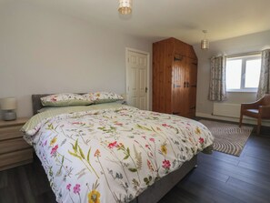 Quarto com cama, guarda-roupa de madeira, cadeira, janela com cortinas e radiador.