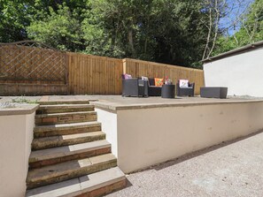 Uma área de pátio com móveis de exterior, cerca de madeira e um conjunto de degraus de concreto que levam a um nível superior.