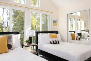 Quarto com duas camas, janelas amplas, um espelho e mesa de cabeceira com abajur.